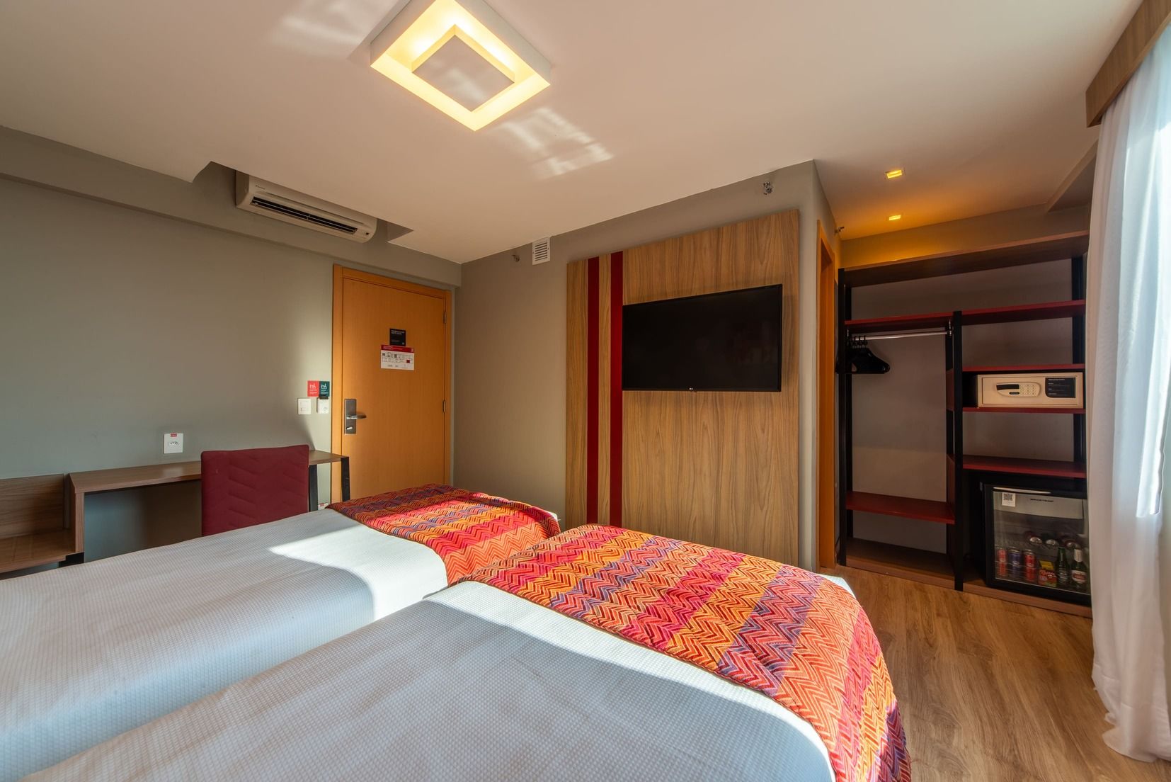 Quarto de hotel com duas camas, uma mesa, televisão, minibar e guarda-roupa.