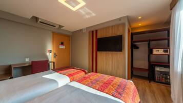 Quarto de hotel com duas camas, uma mesa, televisão, minibar e guarda-roupa.