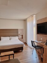 Quarto de hotel com uma cama, uma escrivaninha, uma cadeira, uma televisão e uma janela com cortinas.