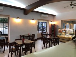 Interior de restaurante com mesas, cadeiras, um balcão de exibição com comida e um ventilador de teto.
