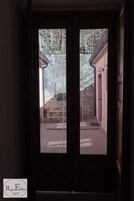 Uma entrada que dá para uma escadaria de pedra com corrimão de metal, um vaso de plantas e um edifício com fachada rosa.
