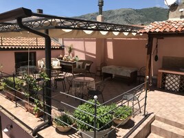 Um pátio com móveis de exterior, plantas em vasos e vista para uma montanha.
