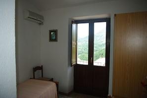 Quarto com cama, cadeira, aparelho de ar condicionado, porta com vista e quadro na parede.