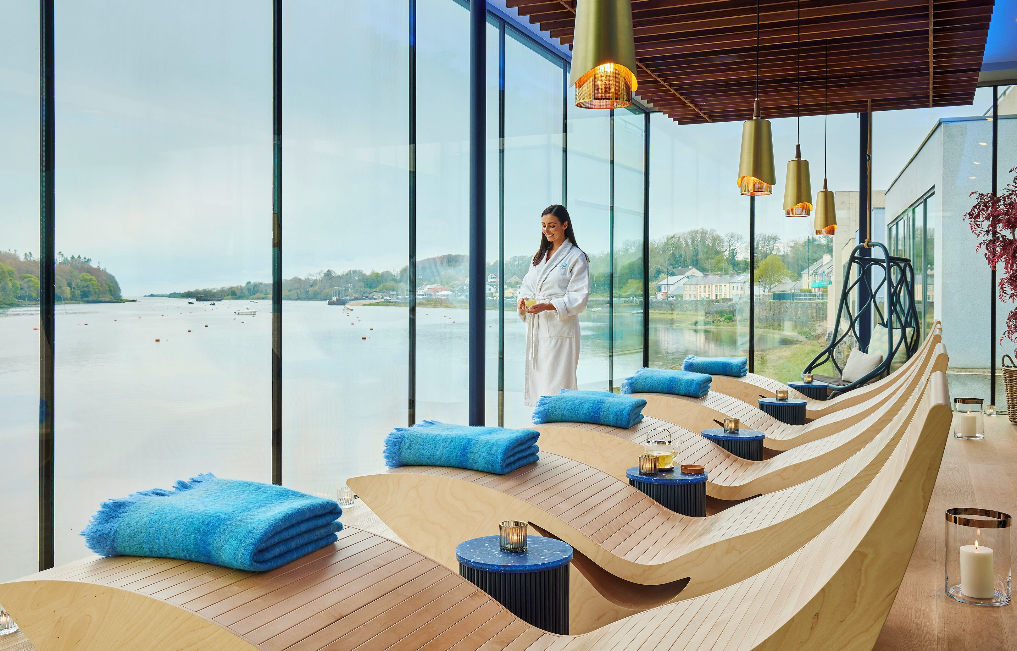 Uma área de spa com espreguiçadeiras de madeira, toalhas azuis e vista para um lago.