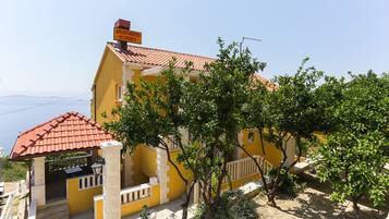 Um edifício amarelo com telhado de telhas vermelhas, uma escadaria que leva à entrada e vista para o mar ao fundo.