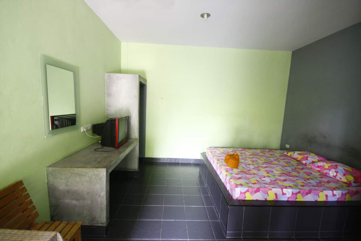 Quarto pequeno e simples com cama, um banco, televisão e espelho.