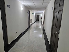 Um corredor comprido e estreito com chão de azulejos, portas em ambos os lados e um extintor de incêndio fixado na parede.