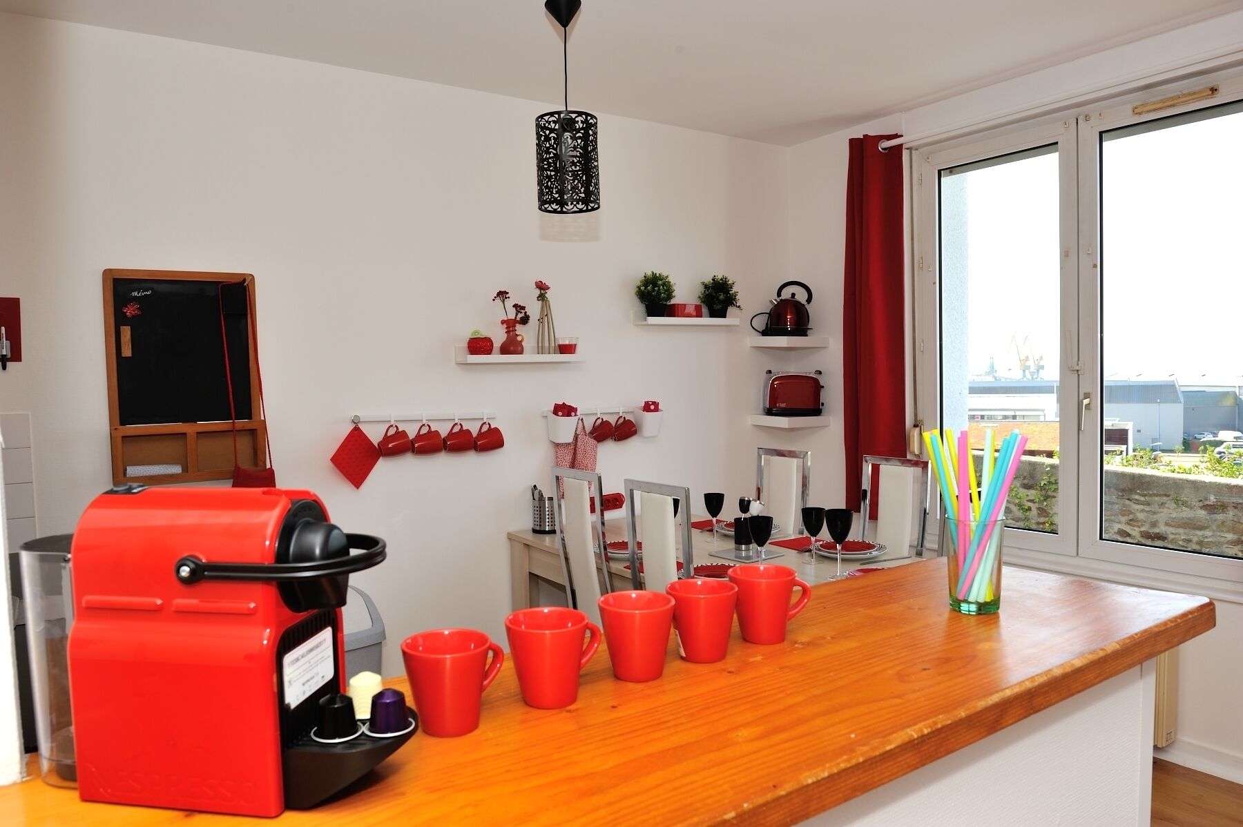 Uma cozinha moderna com uma cafeteira vermelha, canecas vermelhas e uma janela com vista para a cidade.
