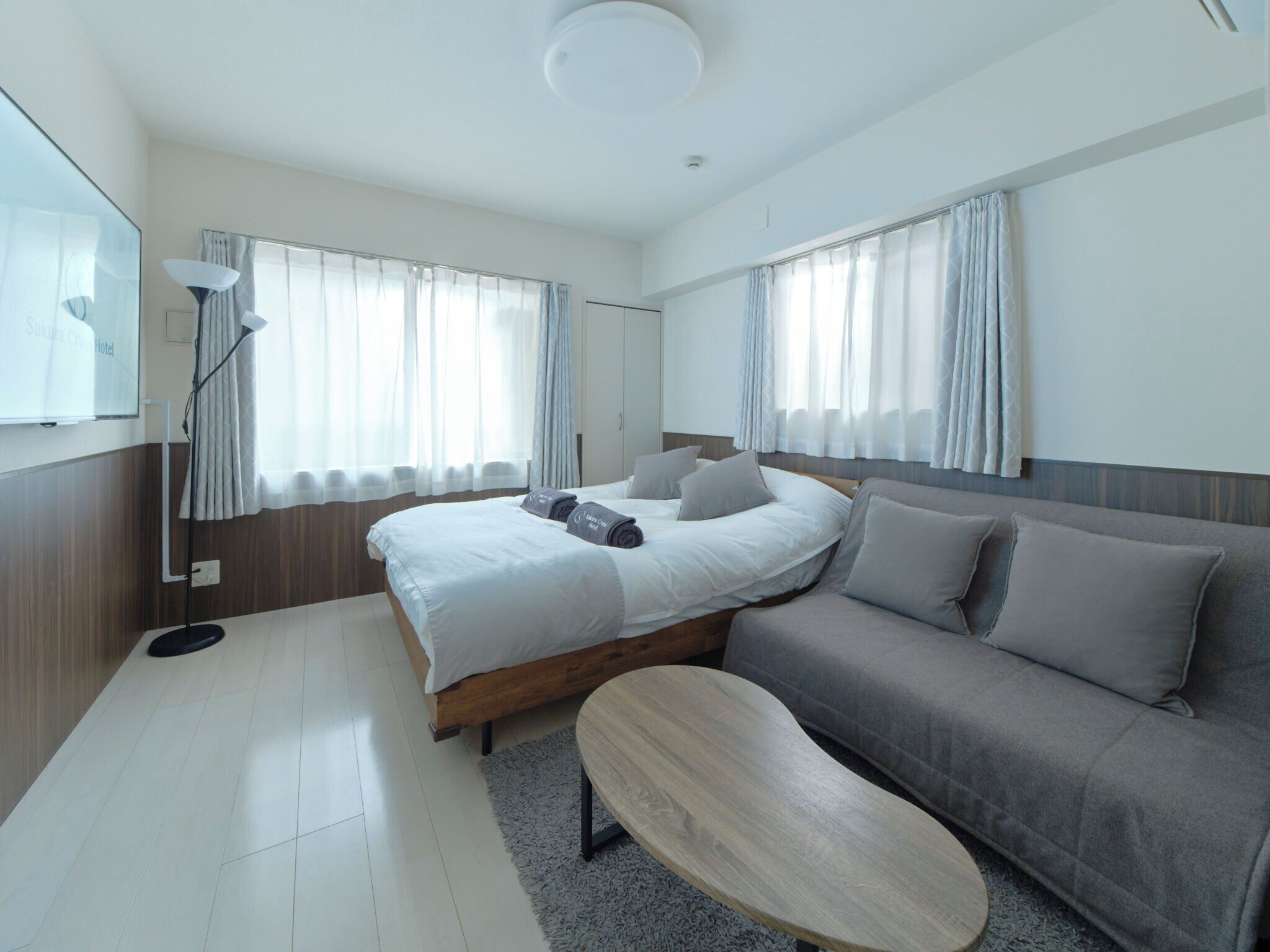 Quarto de hotel moderno com uma cama grande, um sofá, uma mesinha e uma televisão.