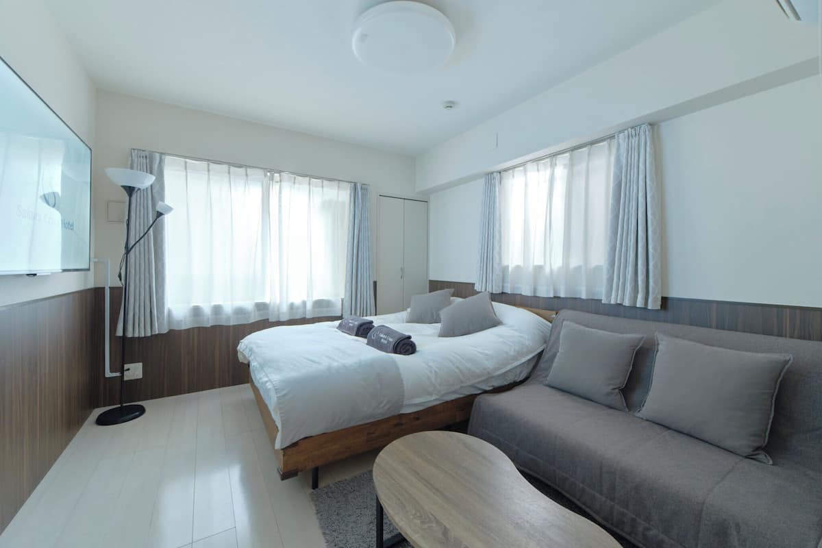 Quarto de hotel moderno com uma cama grande, um sofá, uma mesinha e uma televisão.