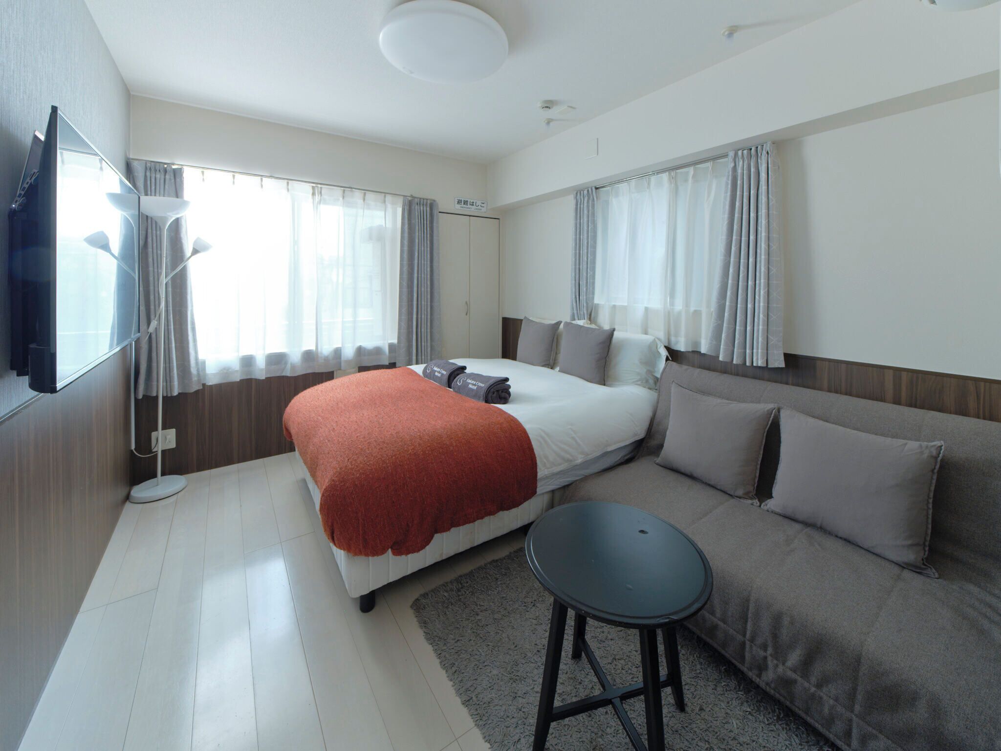 Quarto de hotel com cama, sofá, mesa pequena, televisão e janela com cortinas.