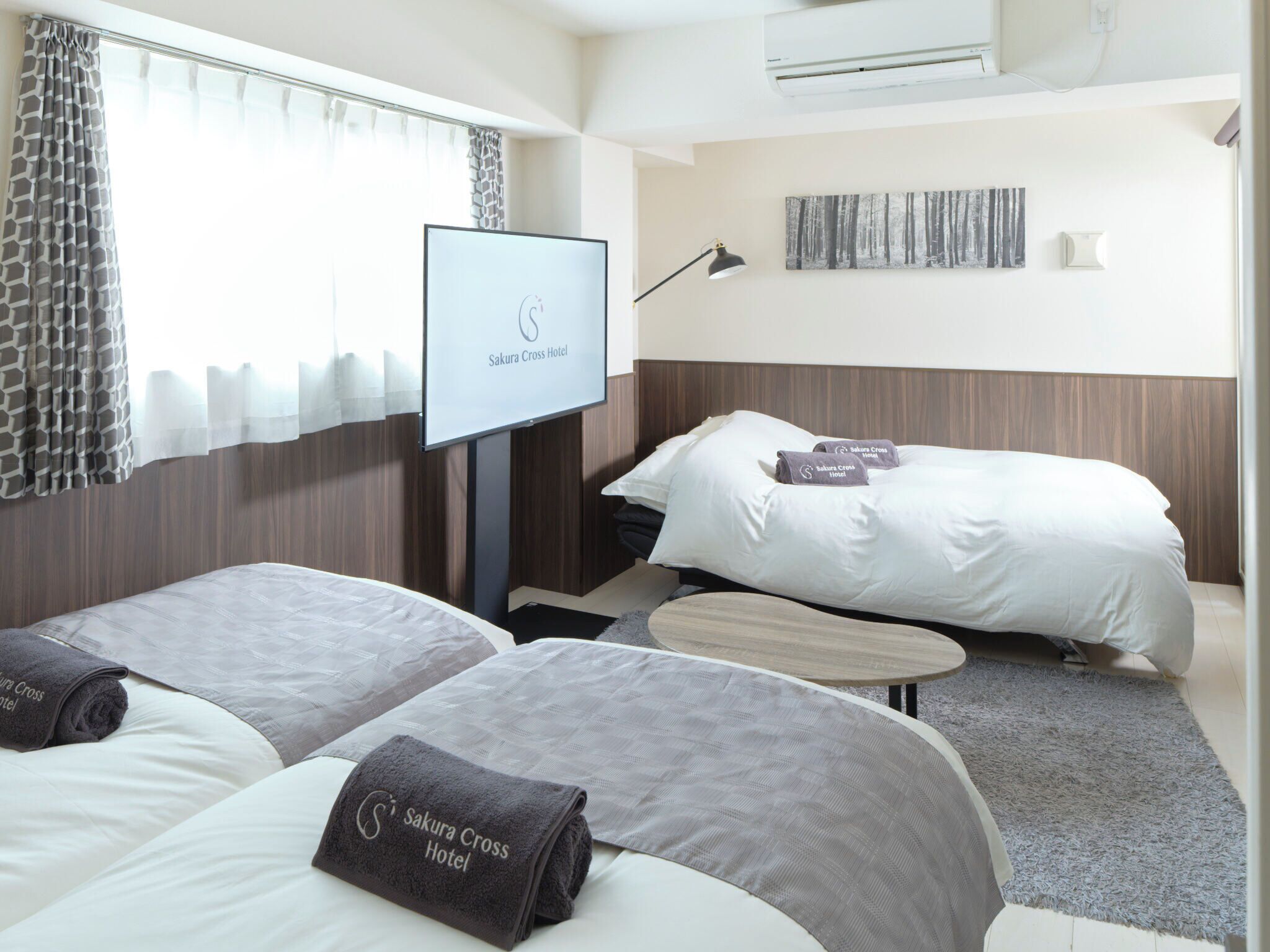 Quarto de hotel com duas camas, televisão, escrivaninha e uma obra de arte na parede.
