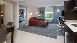 Quarto de hotel moderno com área de jantar, sofá, mesa pequena e TV.