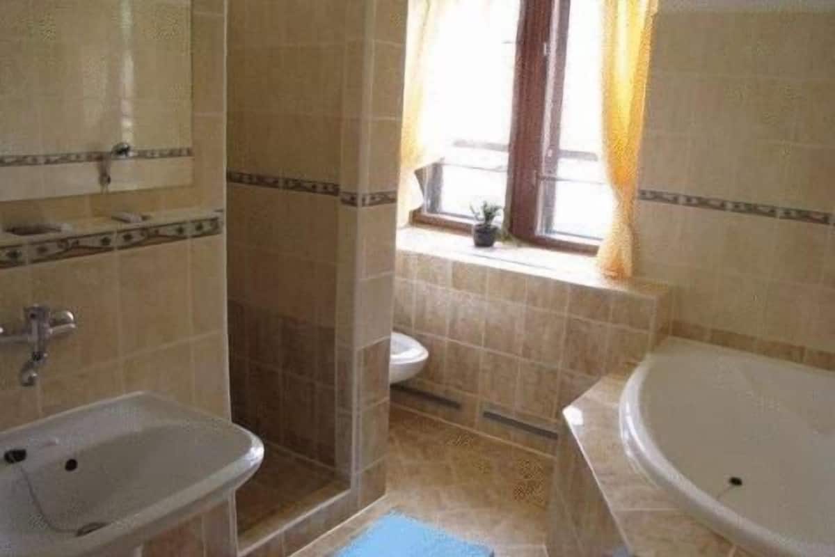 Casa de banho com lavatório, sanita e banheira, com janela e cortinas.