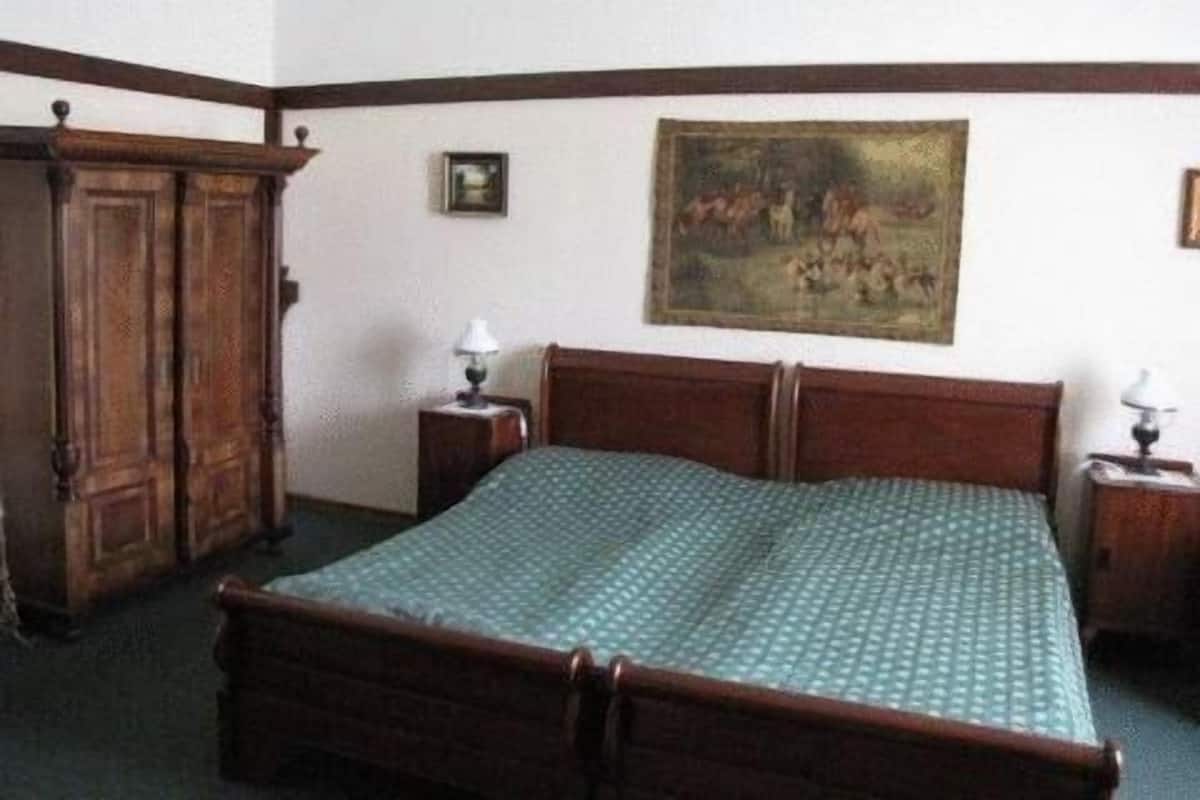 Quarto com cama de madeira, duas mesas de cabeceira, guarda-roupa de madeira e um quadro emoldurado na parede.