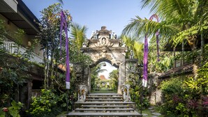 Uma escadaria de pedra leva a uma entrada ornamentada, com estátuas e uma vista desobstruída de um edifício tradicional ao fundo.