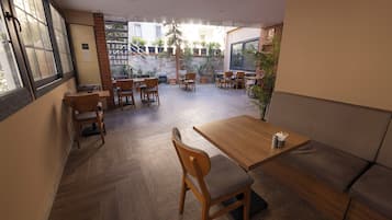 Um restaurante com piso de madeira, várias mesas e cadeiras, um sofá e plantas em vasos.
