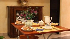 Uma mesa de café da manhã com croissants, um jarro, um bule e um vaso com flores.