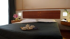 Quarto de hotel com uma cama grande, bandeja com chá e bule, e cabeceira decorativa.