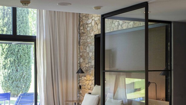 Quarto moderno com uma cama grande, divisória de vidro, parede de pedra e vista para o verde lá fora.