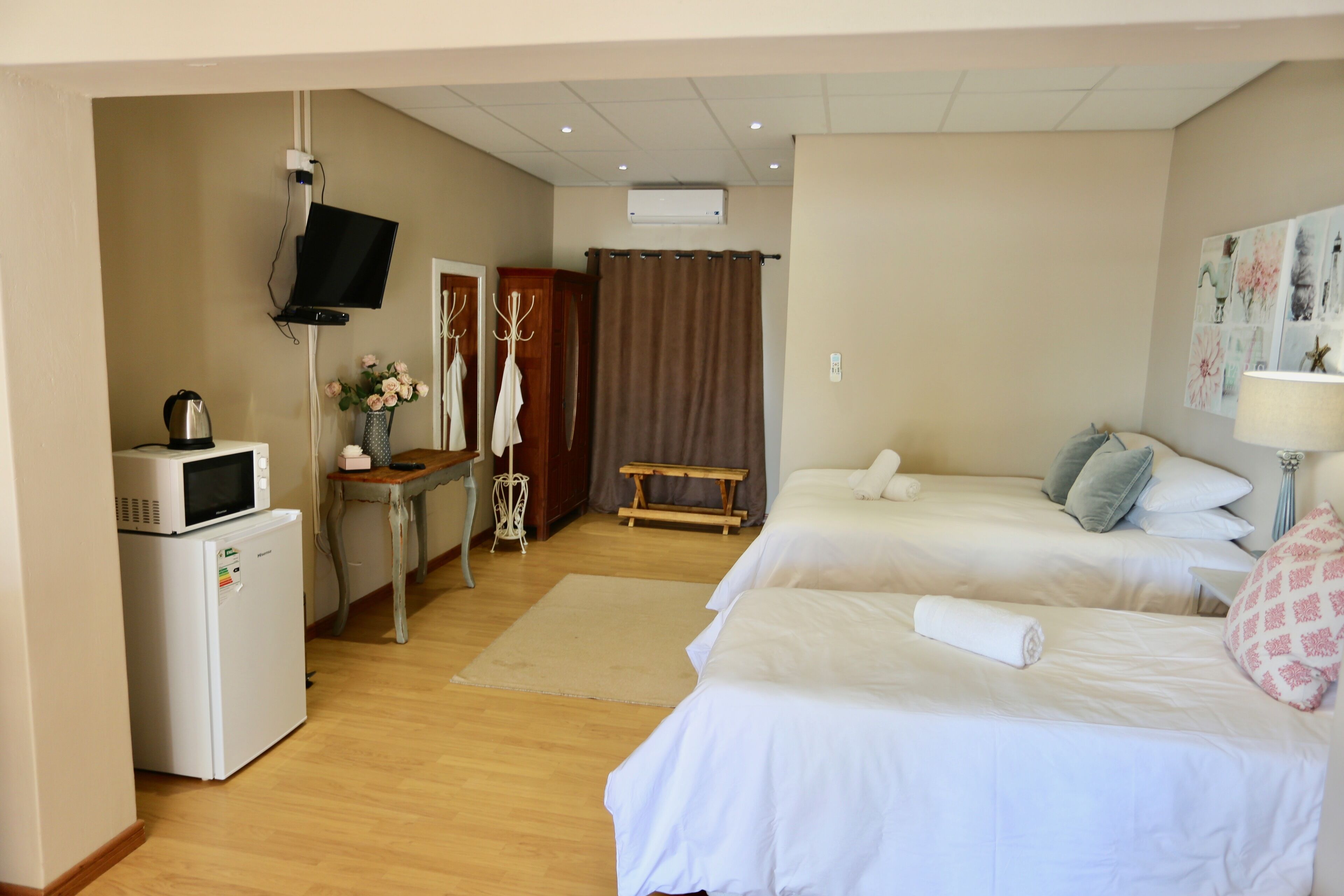 Quarto de hotel com duas camas, uma mesa com computador, micro-ondas, frigorífico, televisão e cortina.
