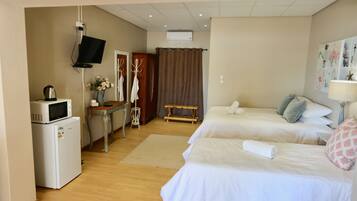 Quarto de hotel com duas camas, uma mesa com computador, micro-ondas, frigorífico, televisão e cortina.