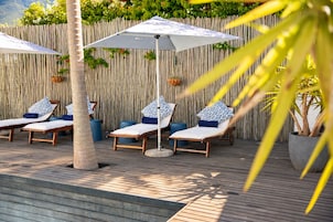 Um deck com cadeiras de lounge e guarda-sóis, cerca de madeira e plantas em vasos.