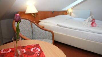 Quarto de hotel com cama, mesa de cabeceira, abajur e um vaso com uma única flor.