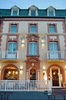 Fachada de hotel com design simétrico, com janelas em arco e varandas, e letreiros iluminados.