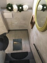 Uma escadaria com carpete preto, uma janela pequena e um espelho na parede.