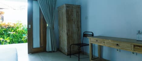 Quarto com escrivaninha de madeira, uma cadeira, guarda-roupa e porta de vidro deslizante para um jardim.