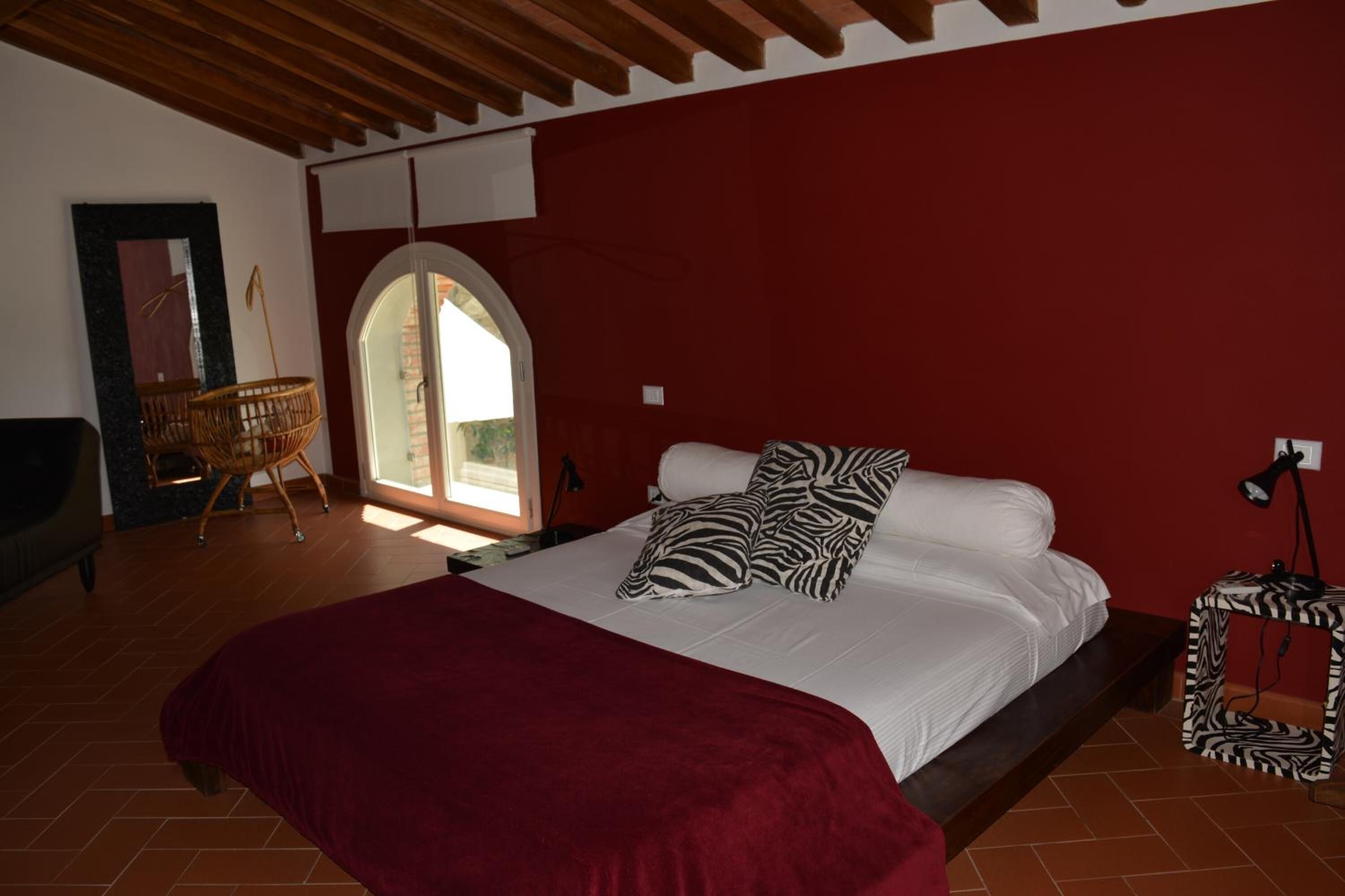 Quarto com cama, parede vermelha, teto de madeira, janela e mesa de cabeceira com padrão de zebra.