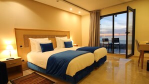 Quarto de hotel com duas camas, varanda, escrivaninha e uma cadeira.