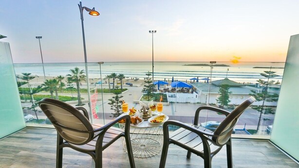 Varanda com mesa posta para o café da manhã, com vista para uma praia e um pôr do sol.