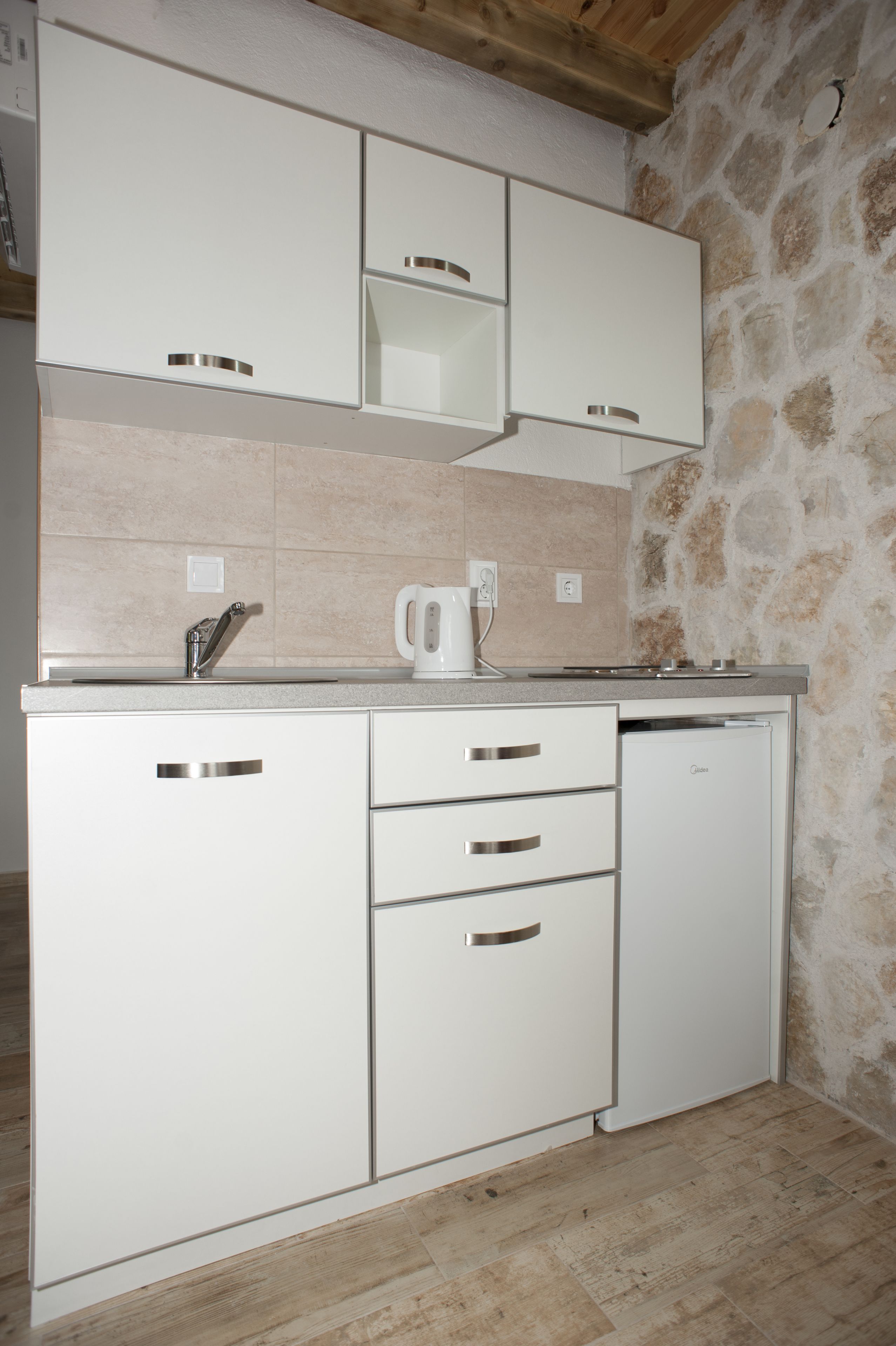 Uma cozinha com armários brancos, lava-louças embutida e parede de pedra.