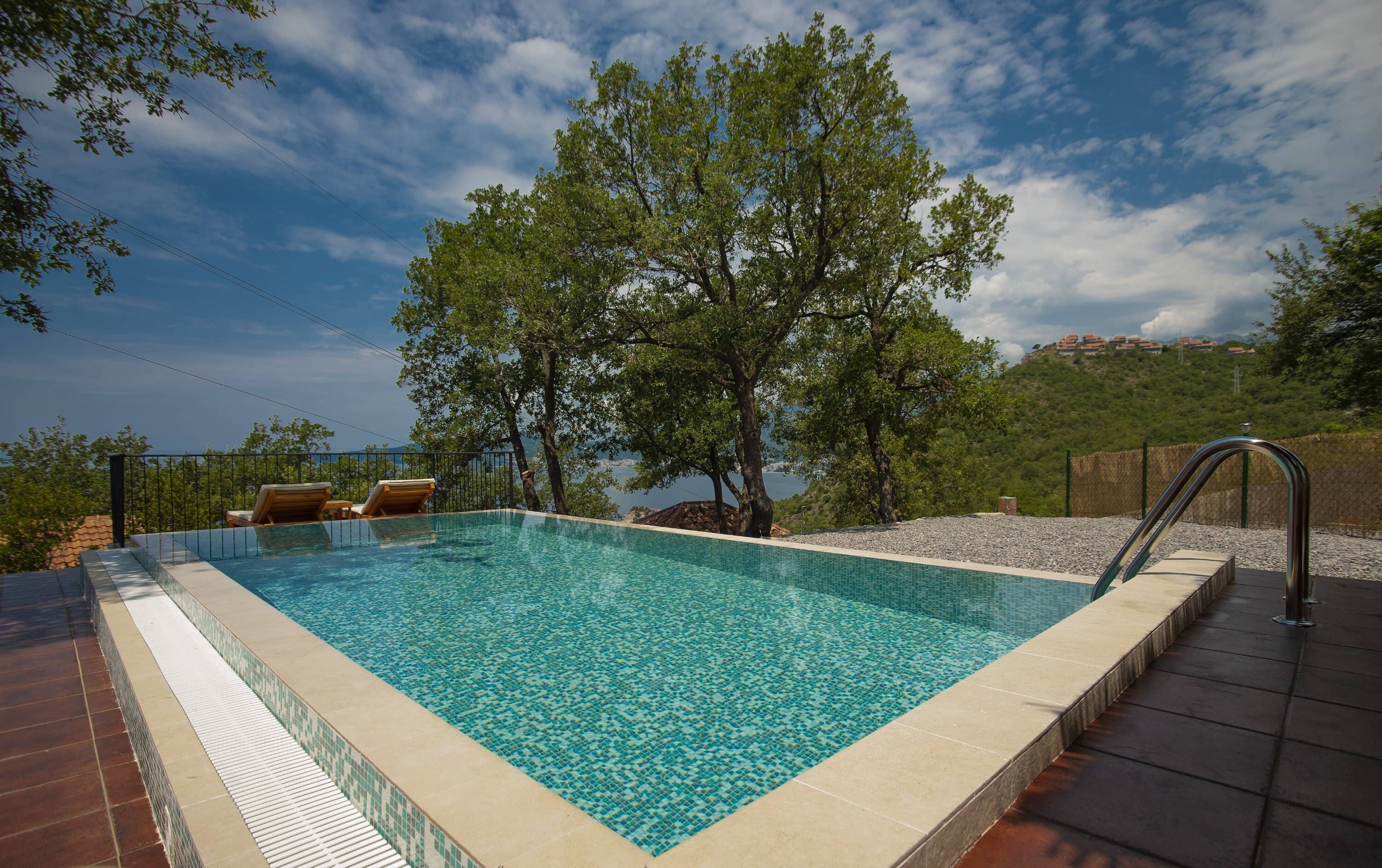 Piscina retangular com borda azulejada, rodeada por um deck com espreguiçadeiras.