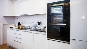 Uma cozinha moderna com armários brancos, forno embutido e bancada de aço inoxidável.