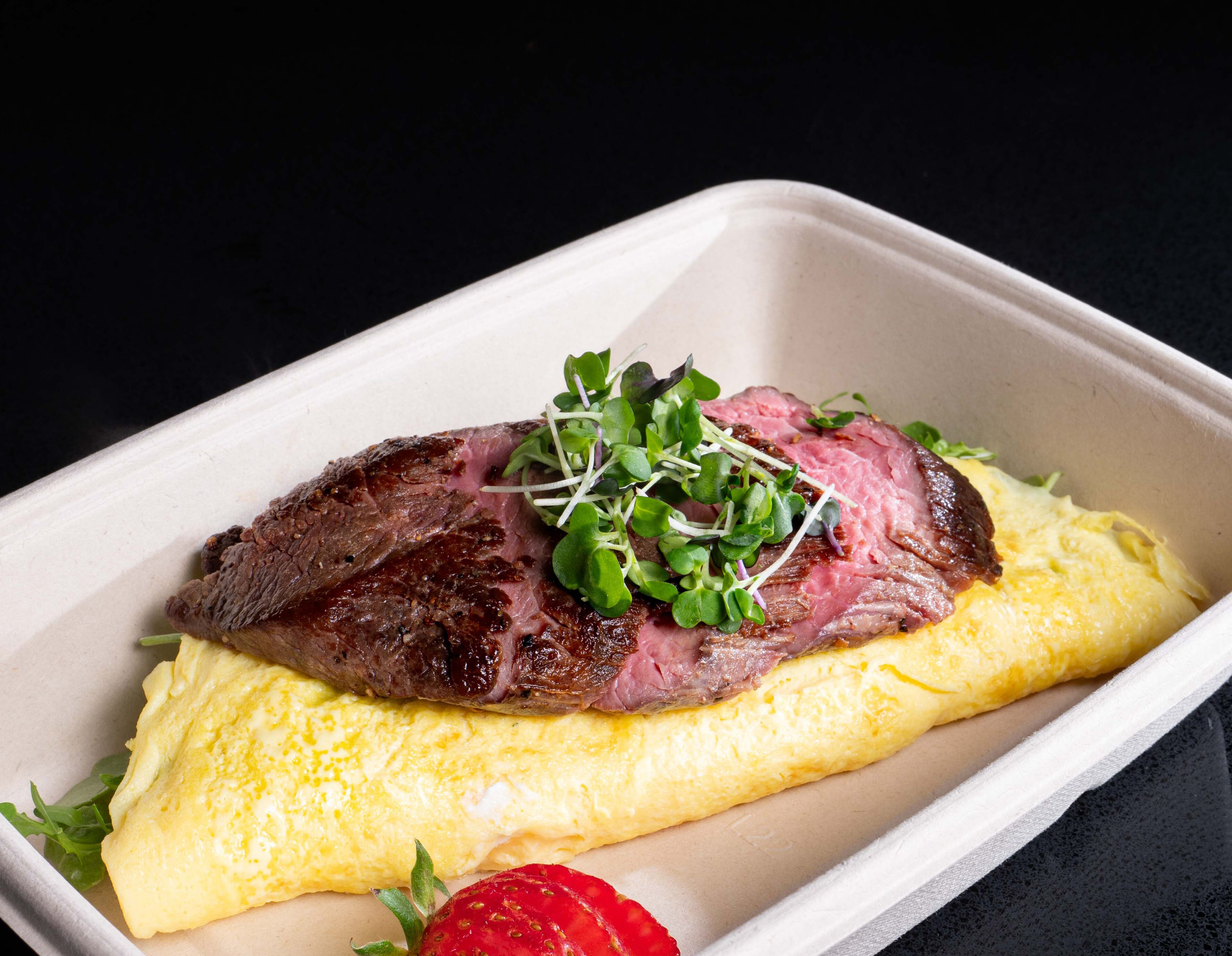 Bife coberto com brotos de microverdes e uma fatia de ovo em um prato retangular.