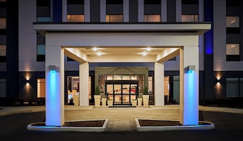 Entrada de hotel com galeria coberta, colunas e porta de vidro que dá acesso ao interior.