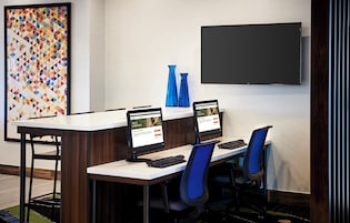 Sala de conferências com uma mesa branca, duas cadeiras, dois monitores e uma grande obra de arte emoldurada na parede.