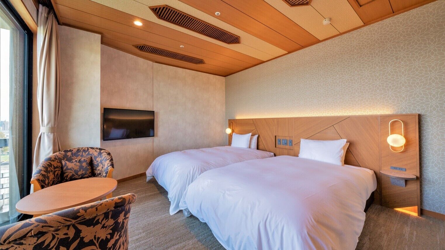 Quarto de hotel com duas camas, televisão de tela plana, uma mesa pequena e uma cadeira.