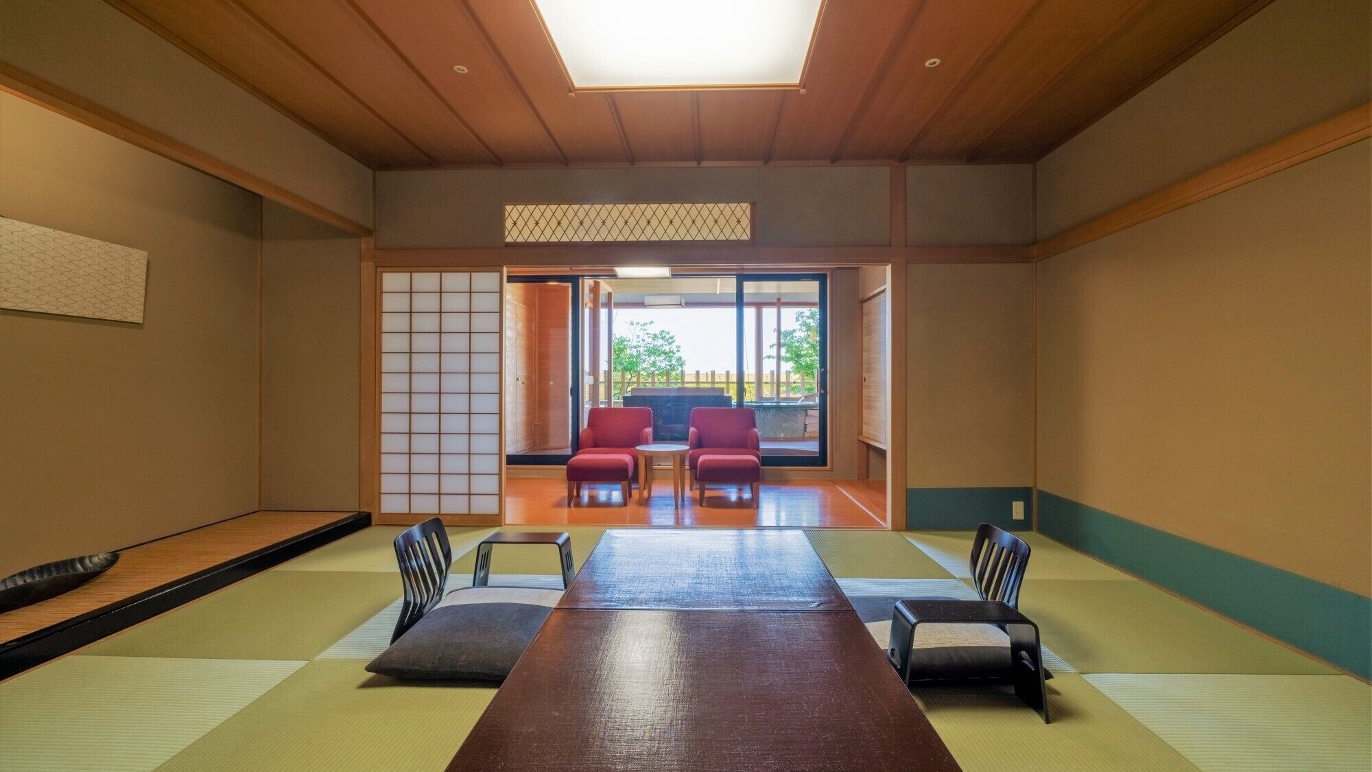 Um quarto japonês tradicional com piso de tatame, uma mesa baixa e cadeiras vermelhas.