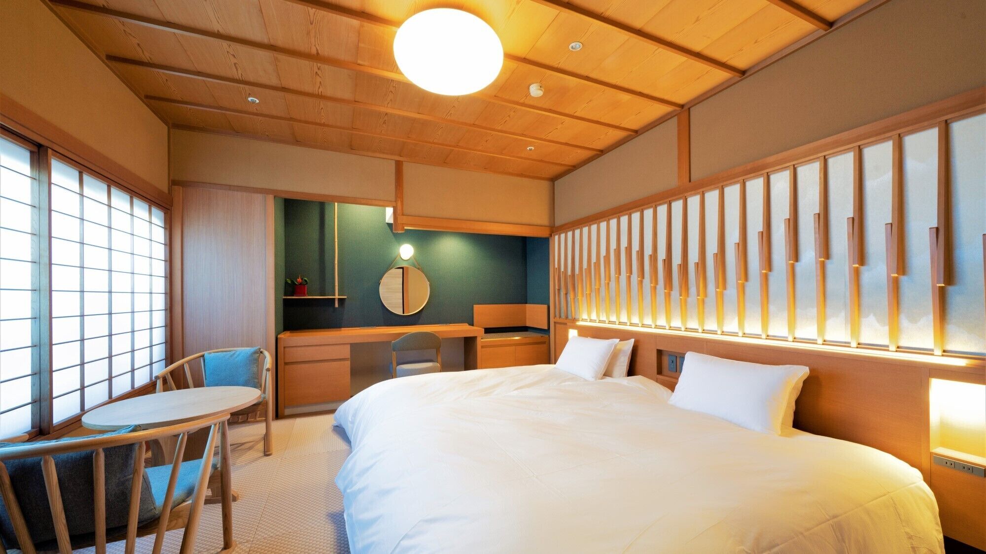 Quarto de hotel com cama, escrivaninha, cadeira e parede com ripas de madeira.