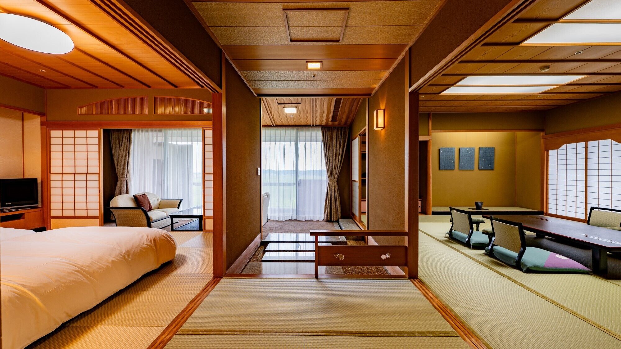 Quarto de hotel em estilo japonês tradicional, com tatames, cama, sofá, mesa de jantar e portas deslizantes.