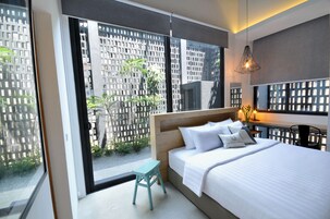Quarto moderno com uma cama grande, um banquinho pequeno e vista para a paisagem urbana através de uma porta deslizante.