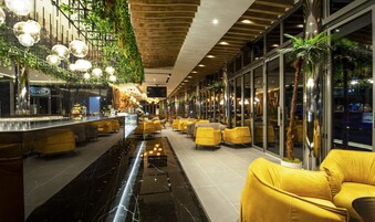 Uma área de bar moderna com piso de mármore, assentos amarelos e uma parede verde com plantas penduradas.