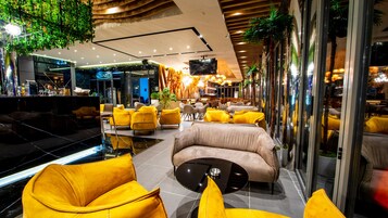 Uma área de lounge moderna com assentos amarelos, uma televisão e um bar com uma placa de neon.