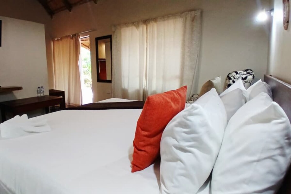 Quarto de hotel com cama, televisão na parede, escrivaninha e janela com cortinas.