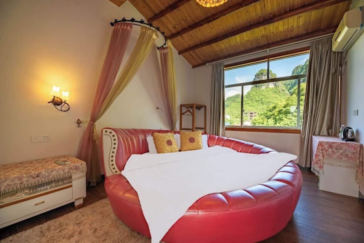 Quarto com uma cama grande, uma cama menor, janela vista para vegetação e um ventilador de teto.