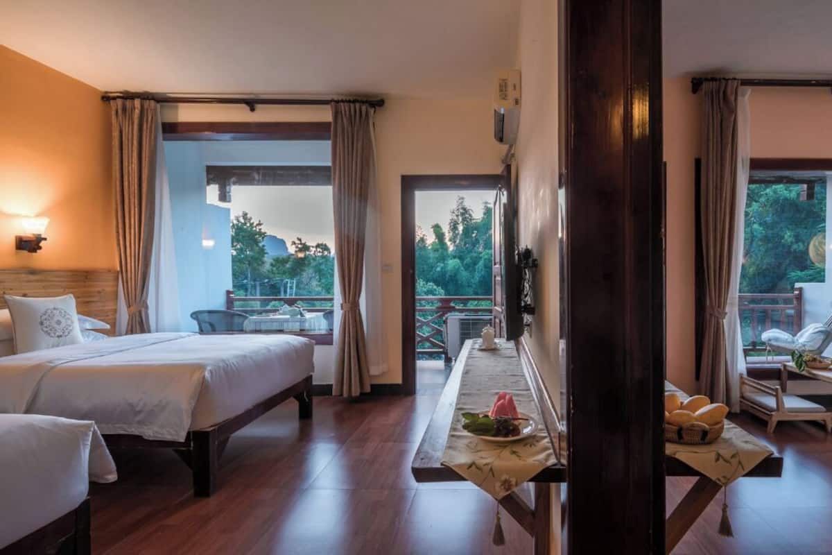 Quarto de hotel com duas camas, uma mesa de jantar com café da manhã e uma varanda com vista.